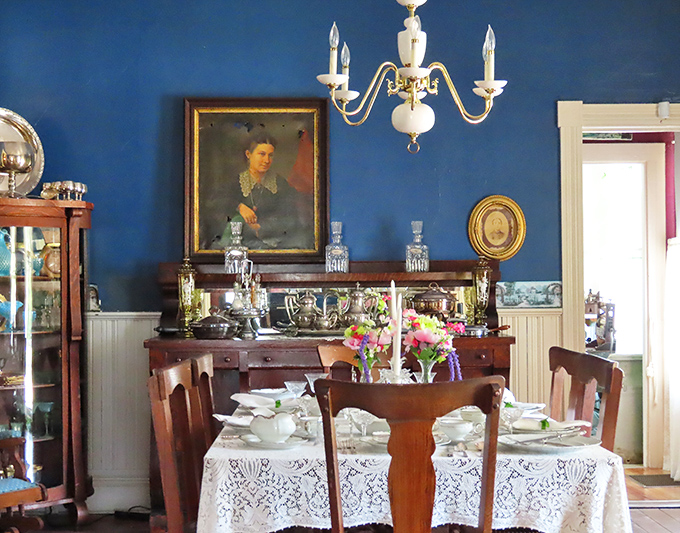 The formal dining room's rich blue walls, white wainscoting, and elegant table setting await phantom dinner guests from another century.