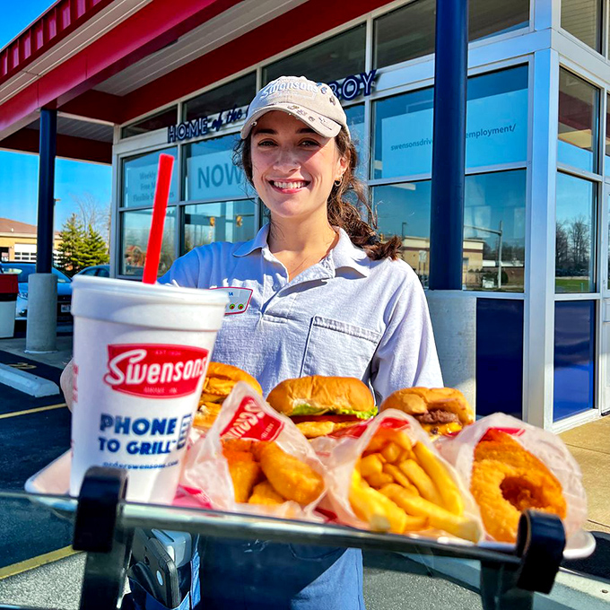A friendly staff member presents a tray loaded with Swensons classics &ndash; the human connection that makes carhop service feel like a warm welcome rather than a transaction.