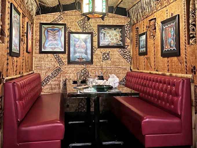 Plush red banquettes create cozy dining nooks surrounded by bamboo walls and tiki art—private islands within the larger tropical paradise.