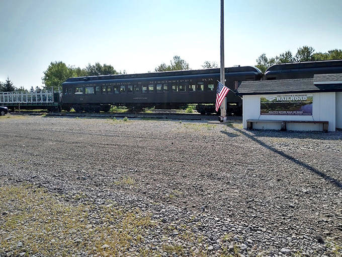 Historic passenger coach stands sentinel beside the station, American flag proudly waving &ndash; a patriotic nod to railroad's role in building America.