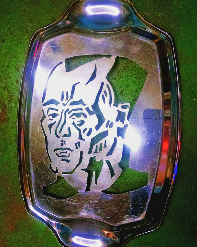 A face emerges from this plasma-cut platter, the metal's reflective surface creating an almost holographic effect that changes with viewing angle.