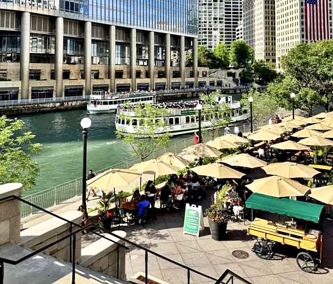 Riverside dining creates memories that linger long after the meal ends, with umbrellas providing shade while boats create an ever-changing waterfront show.