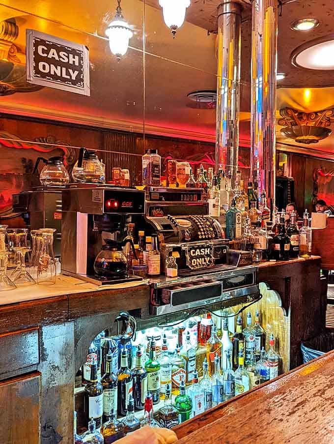 The bar gleams under soft lights, bottles standing at attention like soldiers guarding this fortress of authentic experience.