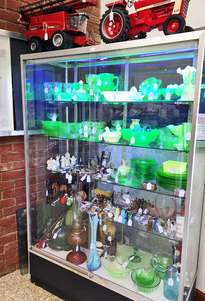 The uranium glass display glows with otherworldly green energy, proving our grandparents casually decorated with materials that now require Geiger counters to identify.