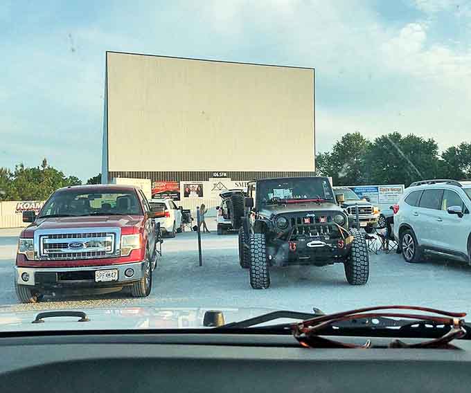 Trucks, SUVs, and sedans gather like a modern-day wagon train, their occupants united by the shared anticipation of the coming feature.