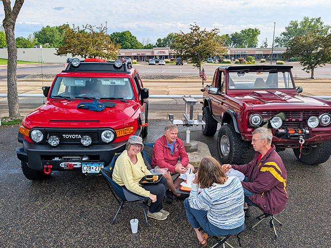 Friends gather beside classic trucks, sharing laughs and drive-in favorites at Minnetonka Drive In, Spring Park, Minnesota today together happily.