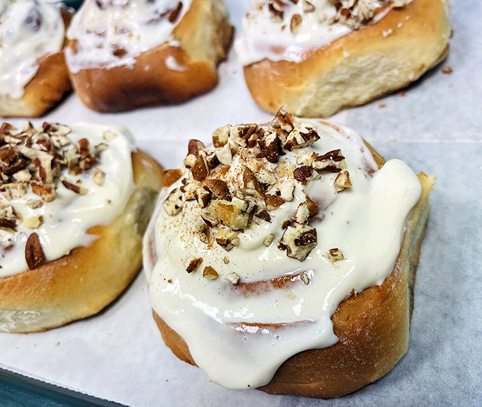 Cinnamon rolls that demand to be unraveled slowly, their cream cheese frosting melting into warm, spiced spirals topped with crunchy pecans.