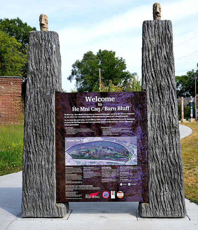 The He Mni Can/Barn Bluff welcome sign stands between wooden sentinels, a gateway to adventure that honors both natural beauty and cultural heritage.
