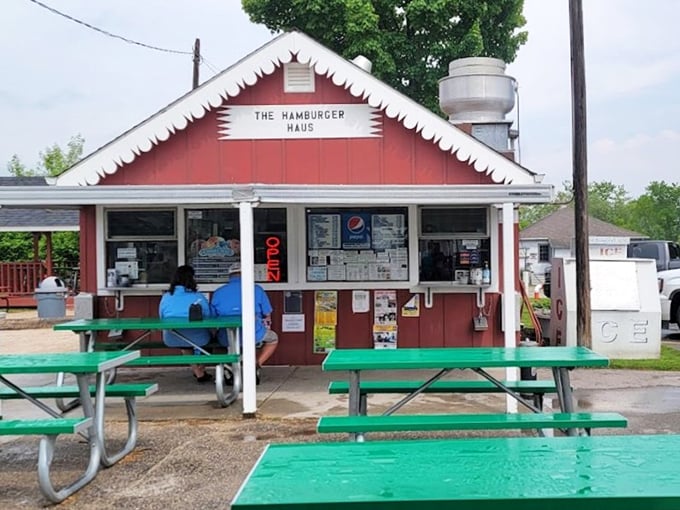 The bright red Hamburger Haus stands ready to serve, with its scalloped trim, glowing OPEN sign, and picnic tables out front inviting diners to enjoy classic roadside fare in the open air.