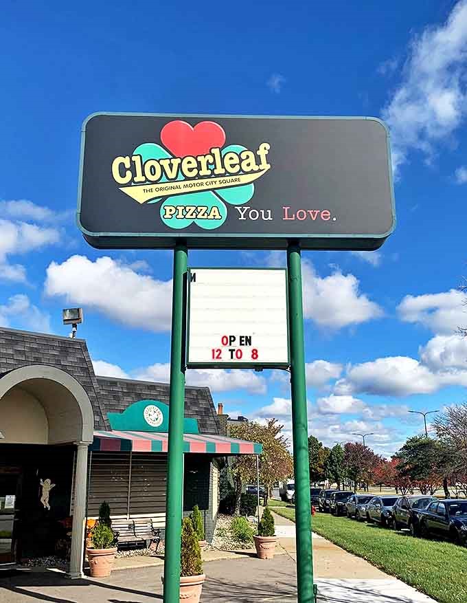 The Cloverleaf sign against blue skies serves as a beacon for pizza pilgrims seeking the holy grail of Detroit-style crust.