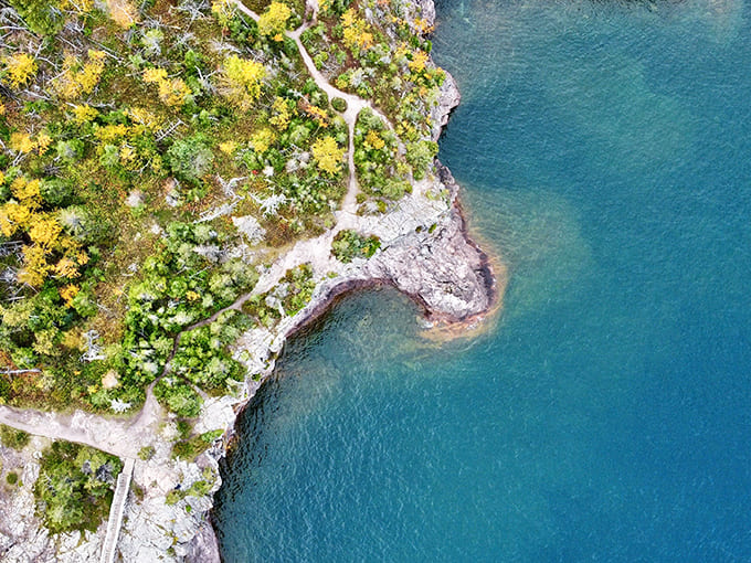Aerial perspective reveals the delicate meeting point of forest and shoreline, where trails wind through pristine wilderness.