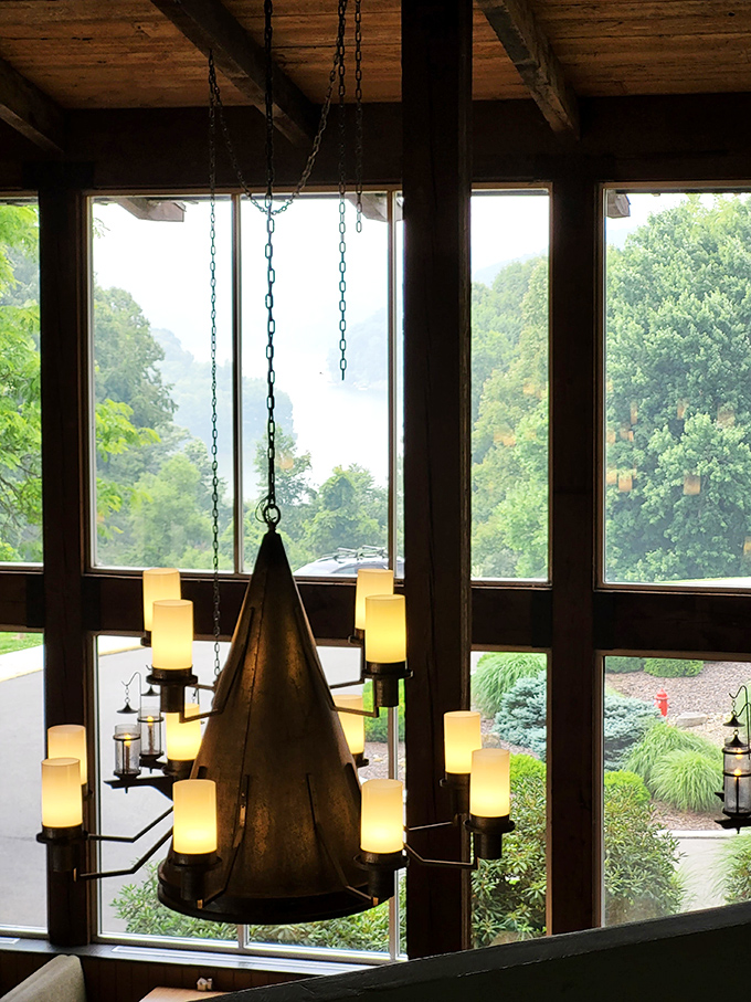 The rustic metal chandelier hangs like an industrial halo, casting warm light through windows that frame nature's ever-changing artwork outside.