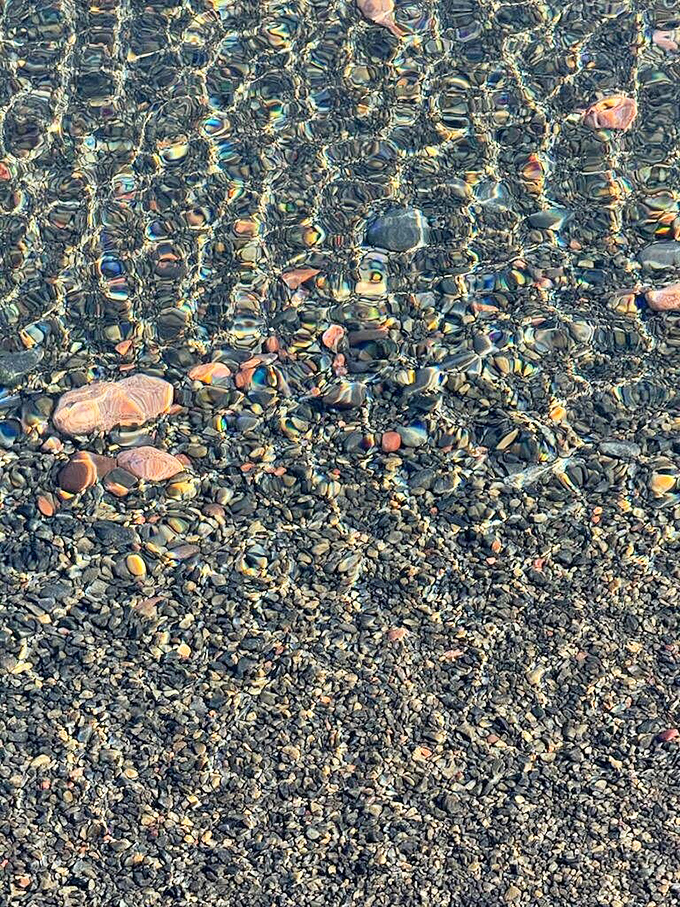 The water's remarkable clarity reveals a kaleidoscope of colorful stones beneath the surface, like nature's own stained glass window.