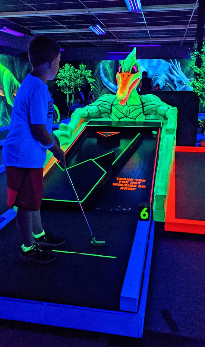 A young golfer faces off against a neon pterodactyl, demonstrating the intense concentration required when putting against extinct predators.