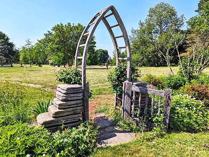 This rustic wooden archway marks the threshold between garden rooms, its weathered frame softened by climbing roses and wild vines.