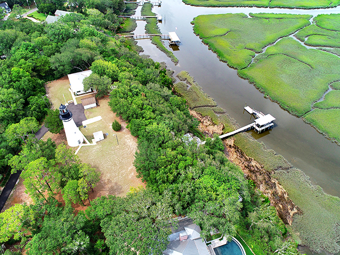An aerial perspective reveals the lighthouse's strategic position between marsh and sea &ndash; a perfect placement for guiding ships home.
