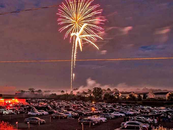 Fireworks illuminate hundreds of cars below, creating a spectacular light show that rivals anything happening on the massive screen.