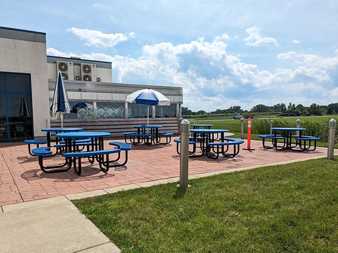 The outdoor seating area provides front-row views of the airfield – blue picnic tables under open skies make for unforgettable dining.