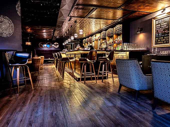 Interior: Warm wood tones and intimate lighting transform this space into a Prohibition-era haven where conversations flow as smoothly as the handcrafted cocktails.