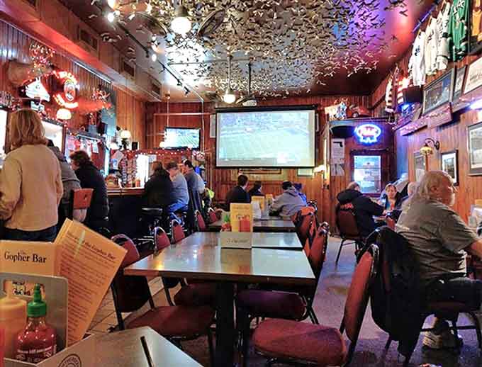 Thousands of dollar bills cling to the ceiling like an upside-down currency carpet, while patrons enjoy the game on screens throughout the wood-paneled haven.