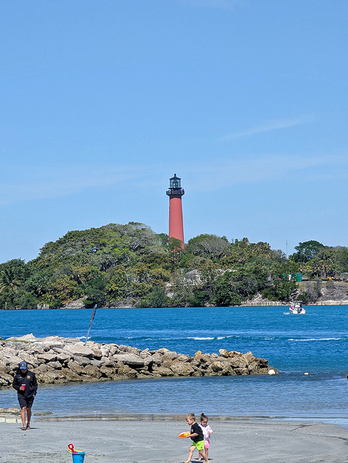 Where turquoise waters meet golden sands, children play while the lighthouse keeps its eternal watch over paradise.