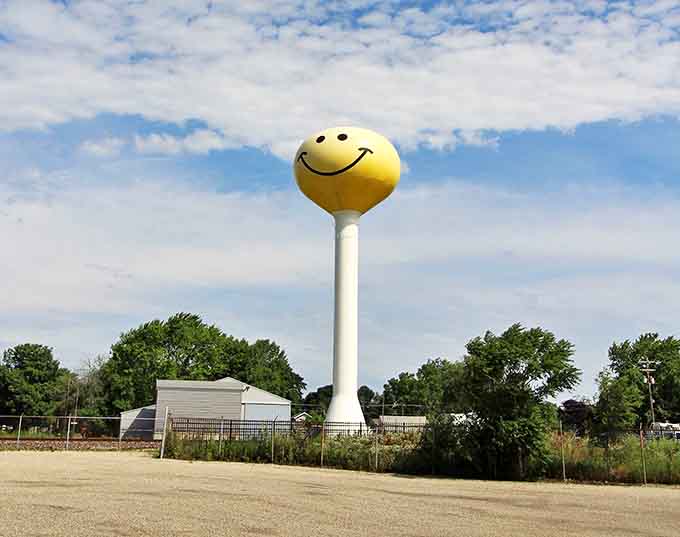 The iconic Smiley Face Water Tower creates a striking silhouette against puffy white clouds, like joy personified in steel and paint.