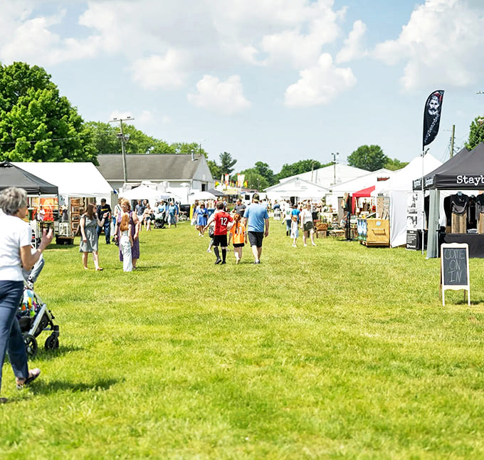 Stalls: Sunlight bathes the grassy pathways between white tents, where families wander in search of that perfect something they never knew they needed.