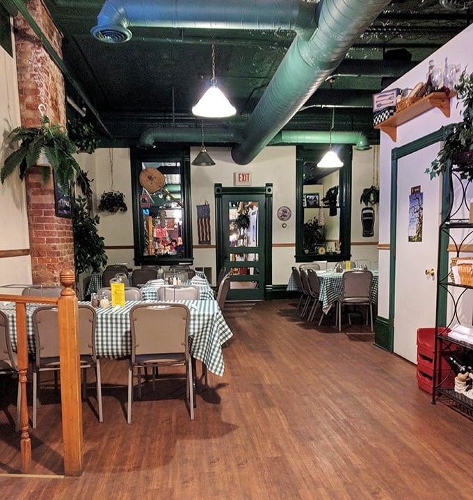 Step inside to discover a cozy dining room with exposed brick, green checkered tablecloths, and an atmosphere that feels delightfully frozen in time.