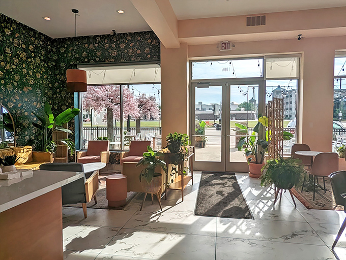 Sunlight streams through large windows, illuminating a botanical paradise where floral wallpaper and lush plants create the perfect backdrop for pastry indulgence.