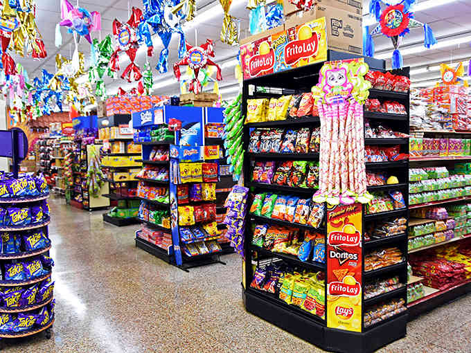 A snack lover's paradise! The aisles burst with vibrant packages of authentic Mexican treats, while pi&ntilde;atas dangle overhead like colorful guardians.