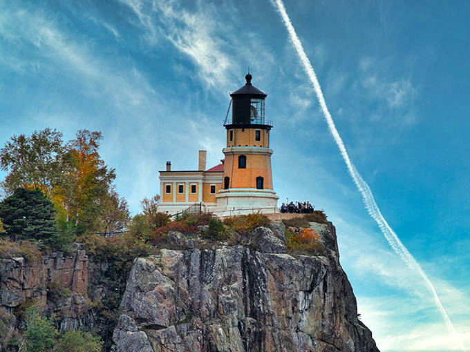 The lighthouse tower reaches skyward against a brilliant blue backdrop, as if trying to high-five passing clouds.