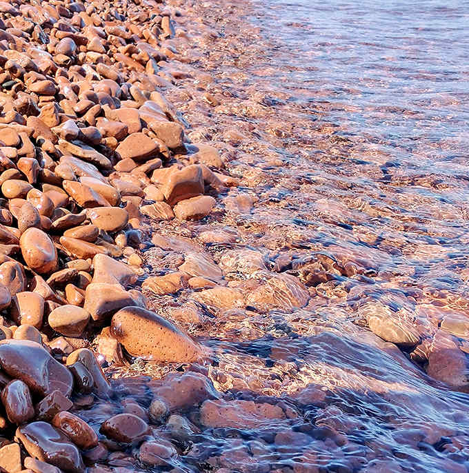 Nature's tumbler at work &ndash; smooth, polished stones create a mesmerizing palette of pinks and reds along the shoreline.