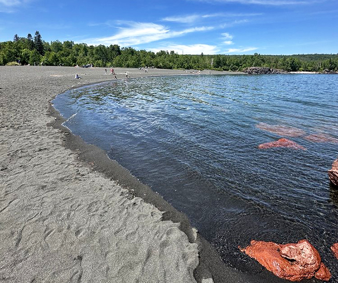 The gentle curve of Silver Bay's shoreline creates a perfect crescent of obsidian sand, like Mother Nature's smile against the blue waters.
