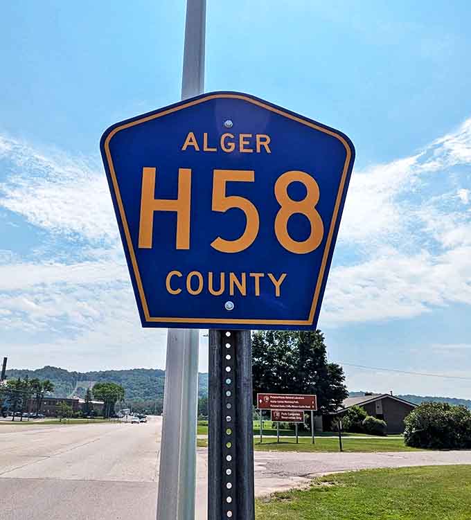 The iconic blue Alger County H-58 sign stands as a gateway to adventure, marking the beginning of Michigan's most spectacular scenic drive.