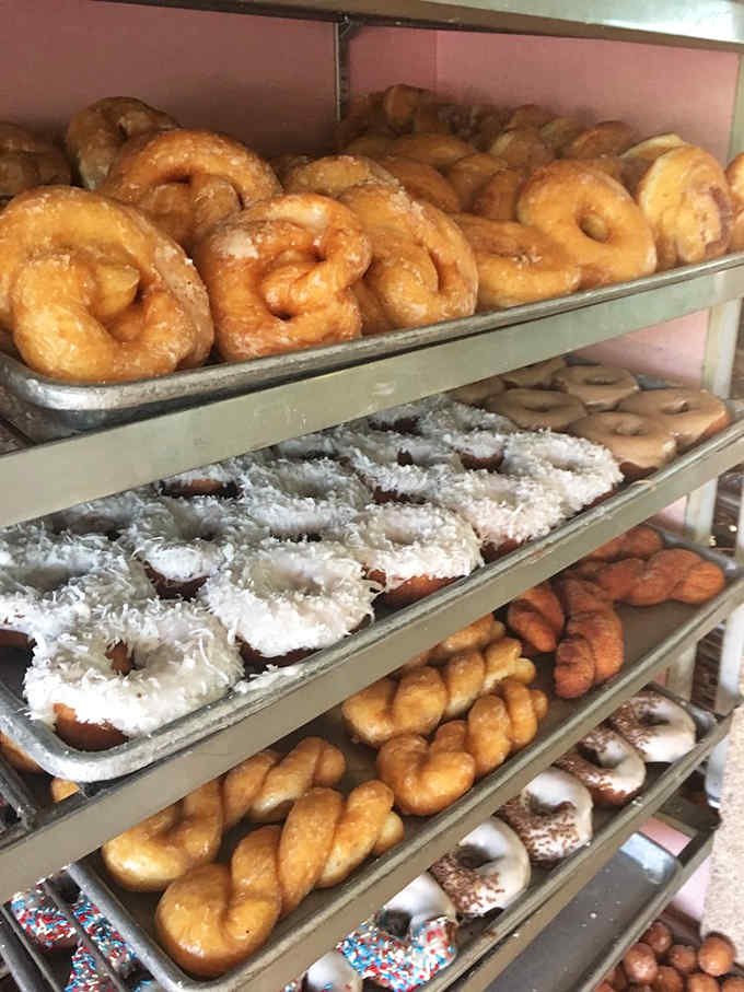 Golden-fried donuts glisten with glaze, arranged in rows that make mathematicians appreciate the beauty of edible geometry.