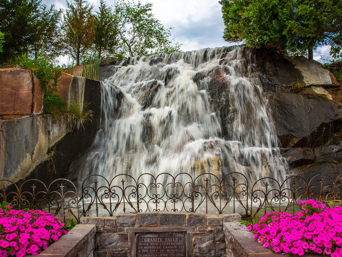 Water dances over stepped granite formations, surrounded by vibrant flowers that add pops of color to this serene setting.