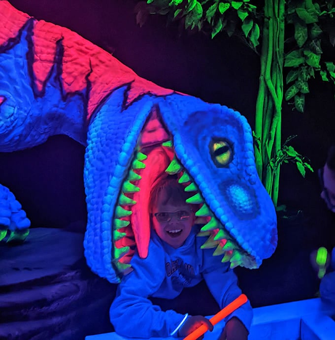 A young adventurer poses inside the jaws of a glowing dinosaur, proving sometimes getting eaten alive can actually be delightful.