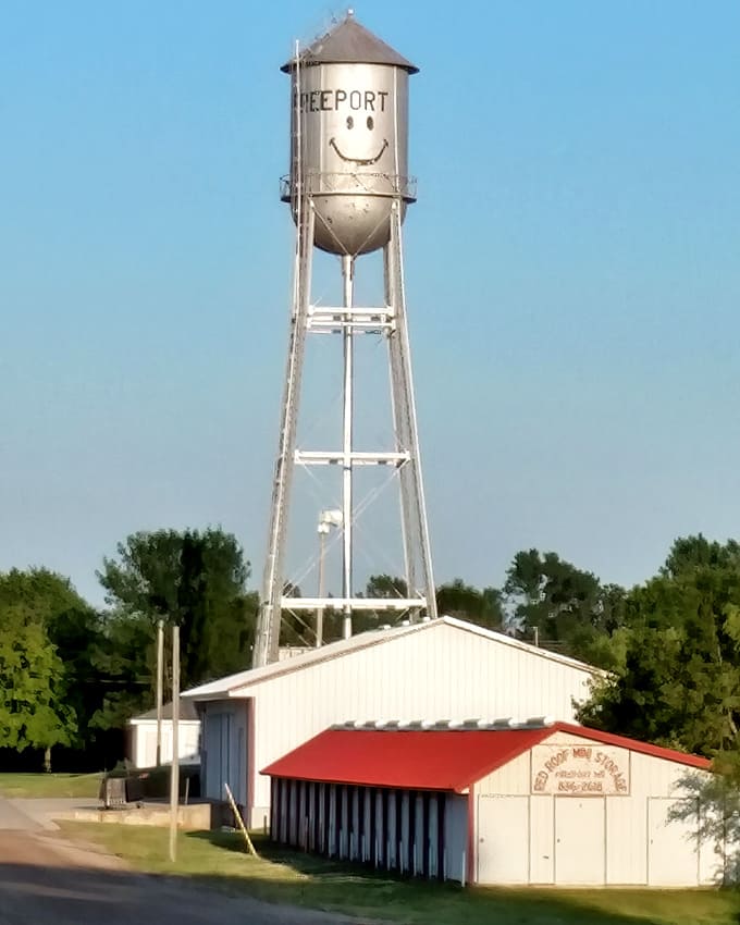 From ground level, the smiling water tower looms large over a small community building, embodying Freeport's blend of practicality and personality.