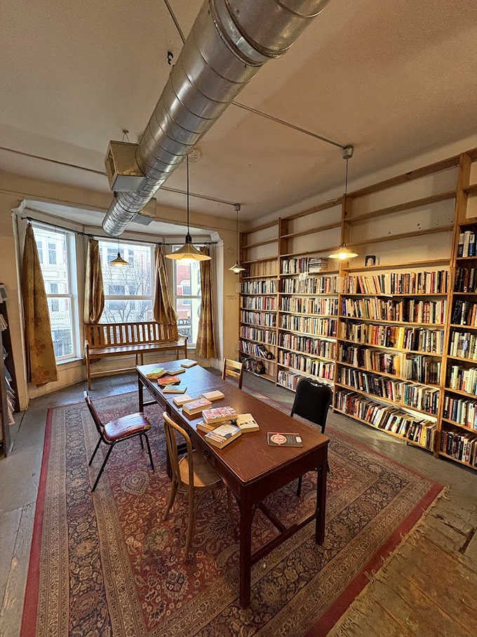 A cozy reading nook bathed in natural light invites visitors to linger, surrounded by thousands of stories competing for attention.
