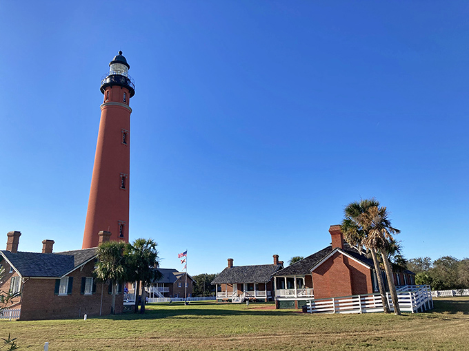 Classic Florida postcard material: the striking red lighthouse tower stands sentinel against a perfect blue sky, surrounded by historic keeper's dwellings that tell tales of maritime history.