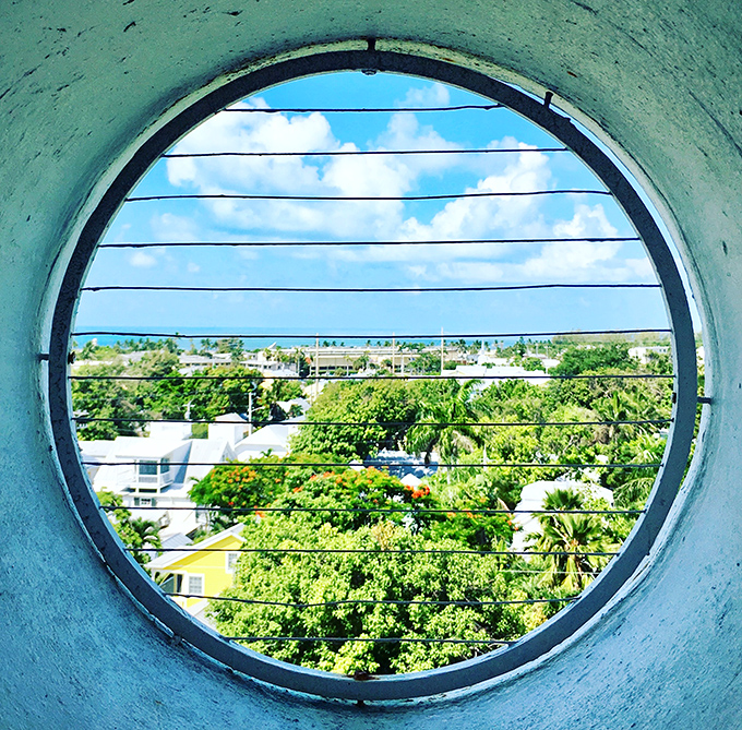 This porthole window frames paradise perfectly, offering a circular glimpse of Key West's lush landscape and azure waters beyond.