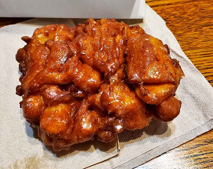 Behold the crown jewel: a single apple fritter with its glorious amber glaze catching the light like stained glass in a cathedral of carbs.