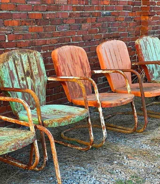 Weathered metal lawn chairs in faded turquoise and orange – silent witnesses to decades of summer conversations and lemonade sipping.