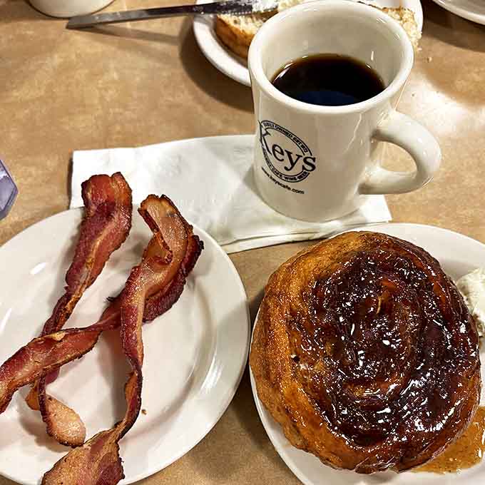 A perfect breakfast trio: crispy bacon, steaming coffee, and the star attraction &ndash; a caramel roll glistening with sweet, sticky goodness.