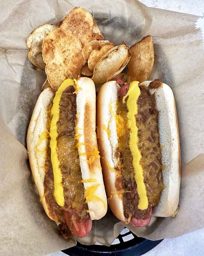 Two perfect Coney Dogs nestled beside golden potato chips &ndash; a simple pleasure elevated to art form.