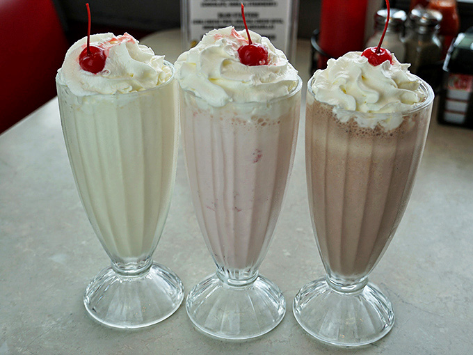 Three milkshakes standing at attention like creamy soldiers, topped with whipped cream clouds and cherries playing king of the mountain.