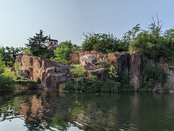 Rugged stone cliffs rise from the crystal-clear quarry waters, crowned with greenery that softens their imposing presence.