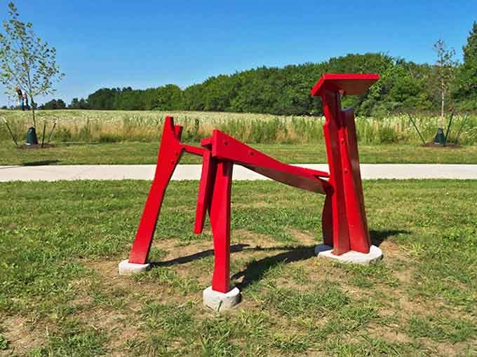 Bold, unapologetic red cuts through green prairie grass &ndash; this sculpture doesn't ask for attention, it demands it with architectural swagger.