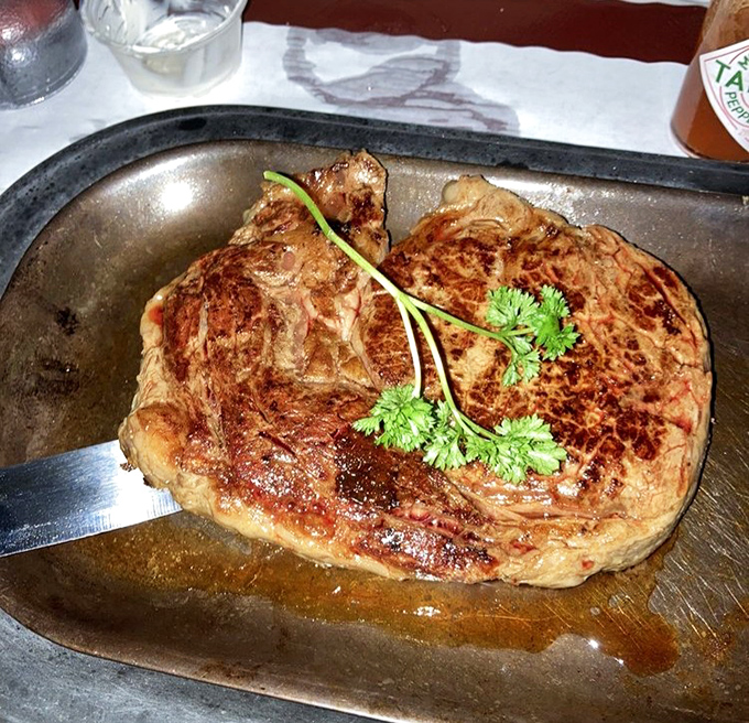 That magnificent ribeye arrives sizzling on its metal platter, a carnivore's dream with perfect caramelization and a sprig of parsley.