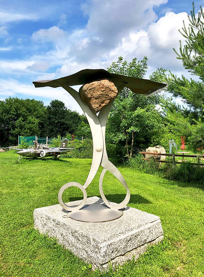 This whimsical "Rock, Paper, Scissors" sculpture defies gravity and expectations, balancing a massive stone above an elegant metal structure.